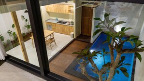 Uma cozinha moderna com armários de madeira, uma área de jantar com mesa e cadeiras, e um pequeno jardim interno com um elemento de água.