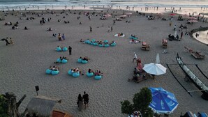 Uma praia com pessoas, cadeiras de praia azuis e guarda-sóis.