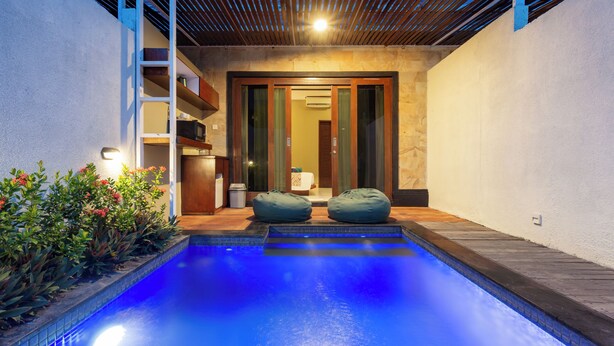 Piscina com dois sacos de feijão, um deck de madeira e uma parede de pedra.