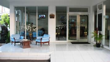 Um saguão de hotel moderno, com balcão de recepção, área de estar e portas de vidro que dão para o interior.