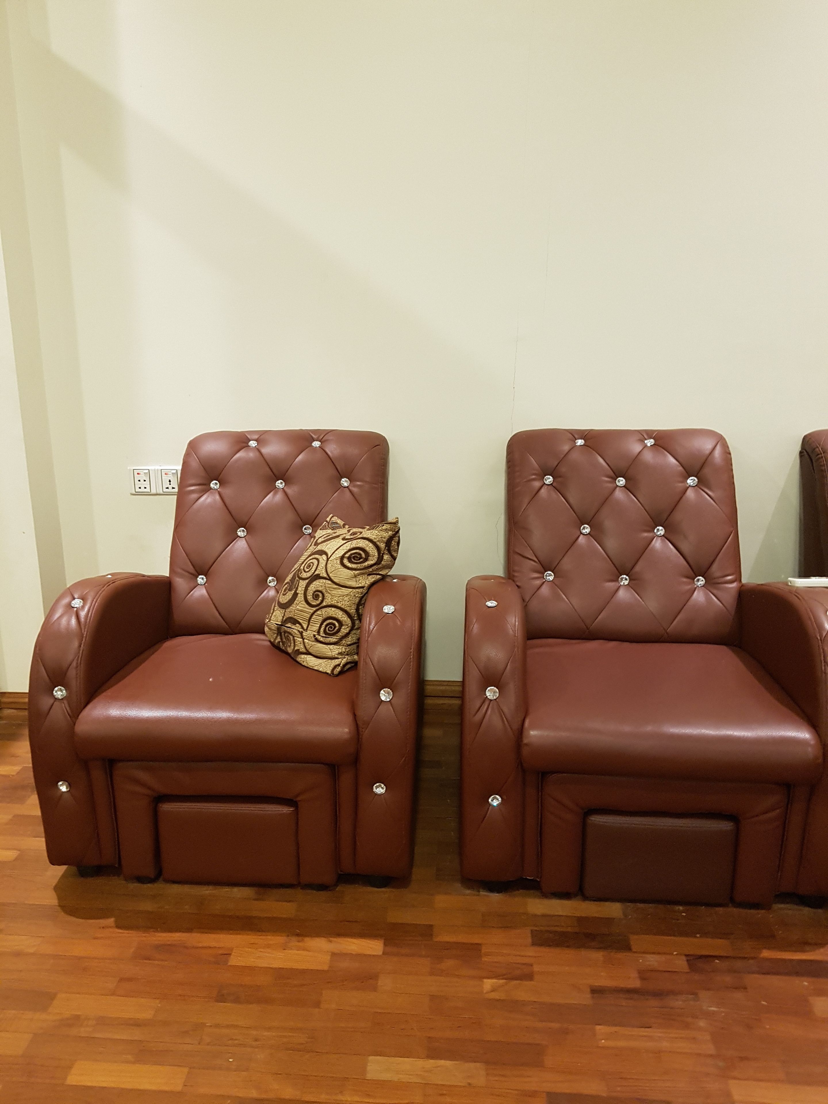 Duas poltronas de couro marrom com encostos e apoio de braços estofados, uma delas com almofada estampada.