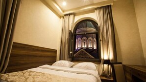Quarto de hotel com uma cama grande, mesa de cabeceira, abajur e janela com cortinas.