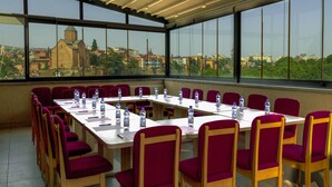 Sala de conferências com uma mesa grande, cadeiras vermelhas e garrafas de água.