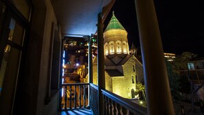 Vista noturna de um edifício com uma torre iluminada e uma varanda com vista para a rua.
