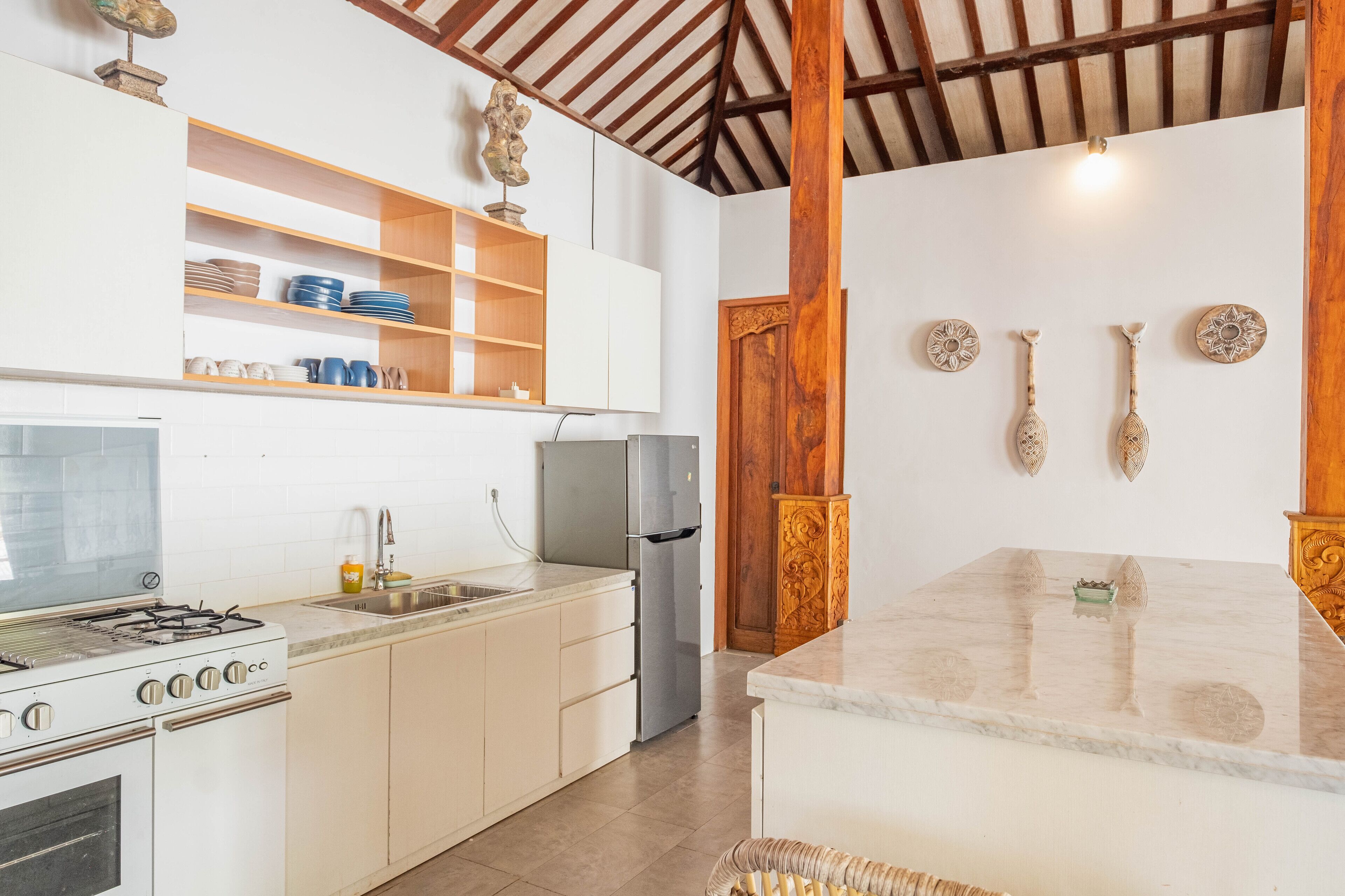 Cozinha com armários brancos, fogão a gás, geladeira e porta de madeira.