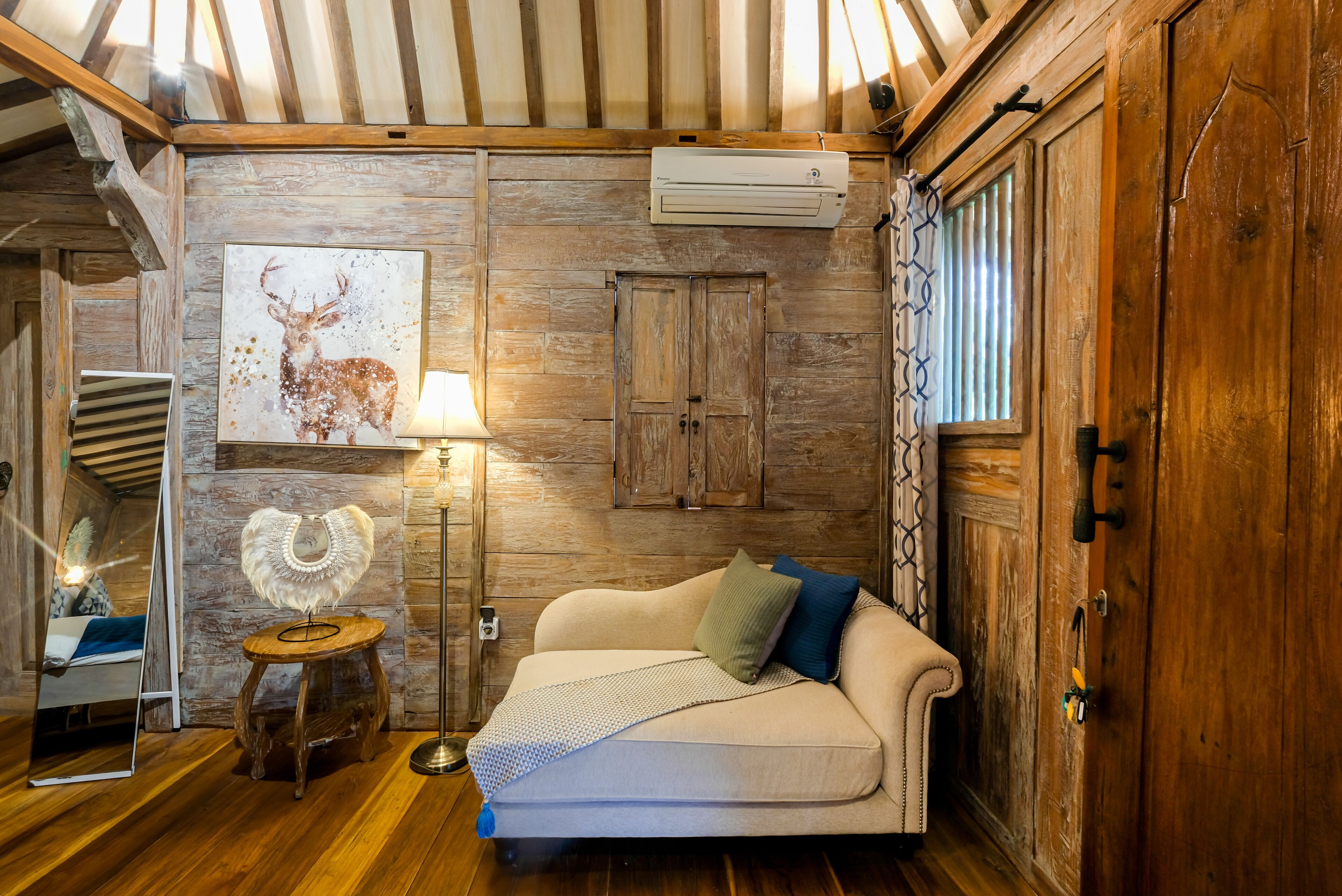 Um quarto acolhedor com teto de madeira, um sofá com almofadas, uma luminária, um ar condicionado fixado na parede e um armário de madeira.