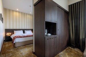 Quarto de hotel com cama, guarda-roupa, mesa de cabeceira e janela com cortinas.