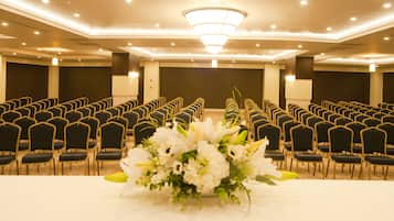 Uma sala de conferências com fileiras de cadeiras, uma mesa com arranjo floral e uma área de palco.