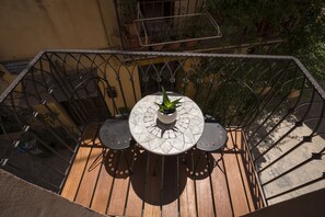 Um deck de madeira com uma mesa redonda e duas cadeiras, cercado por um guarda-corpo de metal.