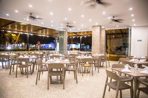 Um restaurante com várias mesas e cadeiras, ventiladores no teto e vista para o exterior.