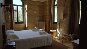 Quarto de hotel com uma cama grande, uma cadeira, uma escrivaninha e um abajur.
