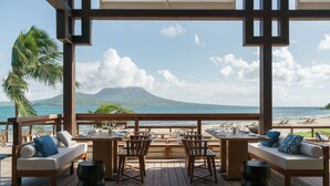 Um deck de madeira com assentos externos, vista para o oceano e uma montanha ao fundo.