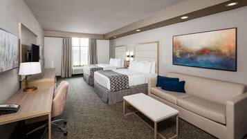 Quarto de hotel com duas camas, uma escrivaninha com luminária, um sofá, uma mesa de centro e uma grande pintura abstrata na parede.