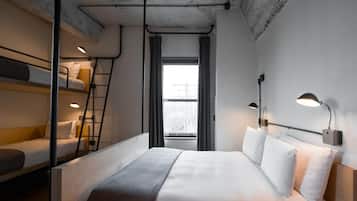 Quarto com beliche, uma cama grande com cabeceira, duas luminárias de mesa e uma janela com cortinas.