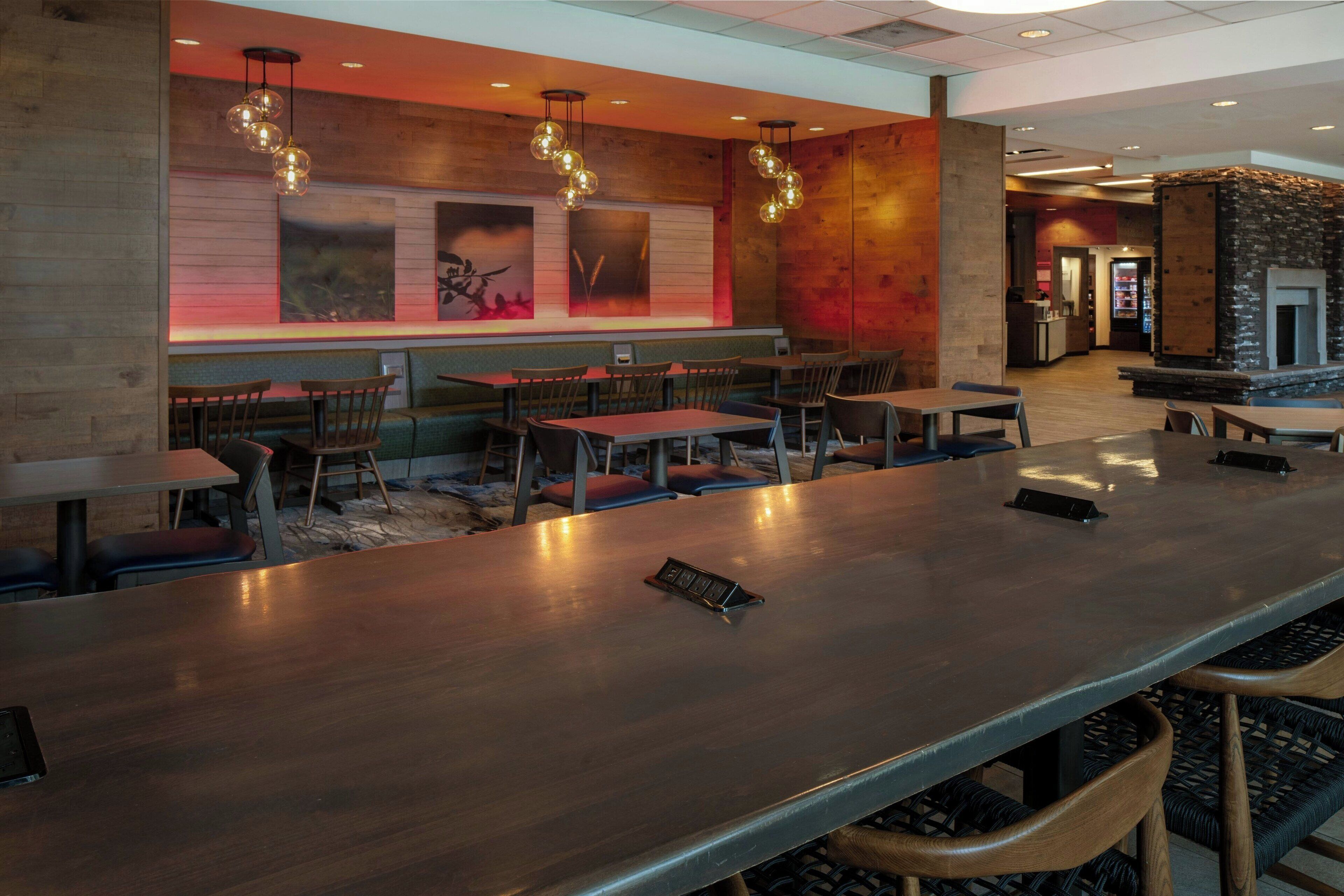 Um restaurante moderno com uma longa mesa comunitária, cabines e luminárias pendentes.