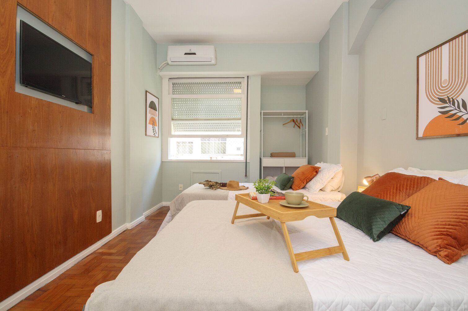 Quarto com cama, mesa de cabeceira e televisão na parede.