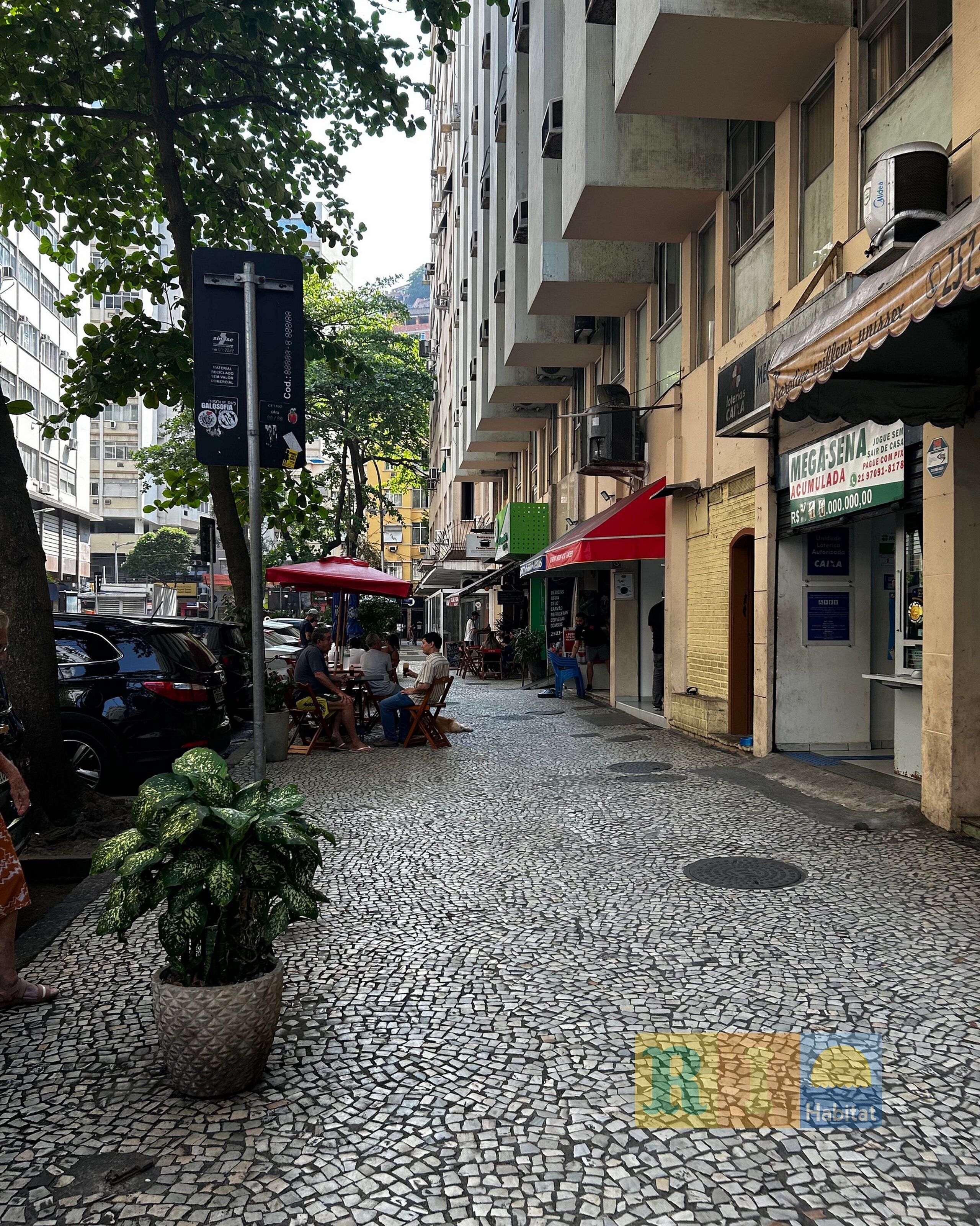 Uma rua de paralelepípedos com edifícios, um guarda-chuva vermelho e uma placa com a inscrição 'MEGA SENA'.