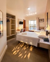 Quarto de hotel com uma cama, uma escrivaninha, uma cadeira, uma televisão e uma janela com vista.