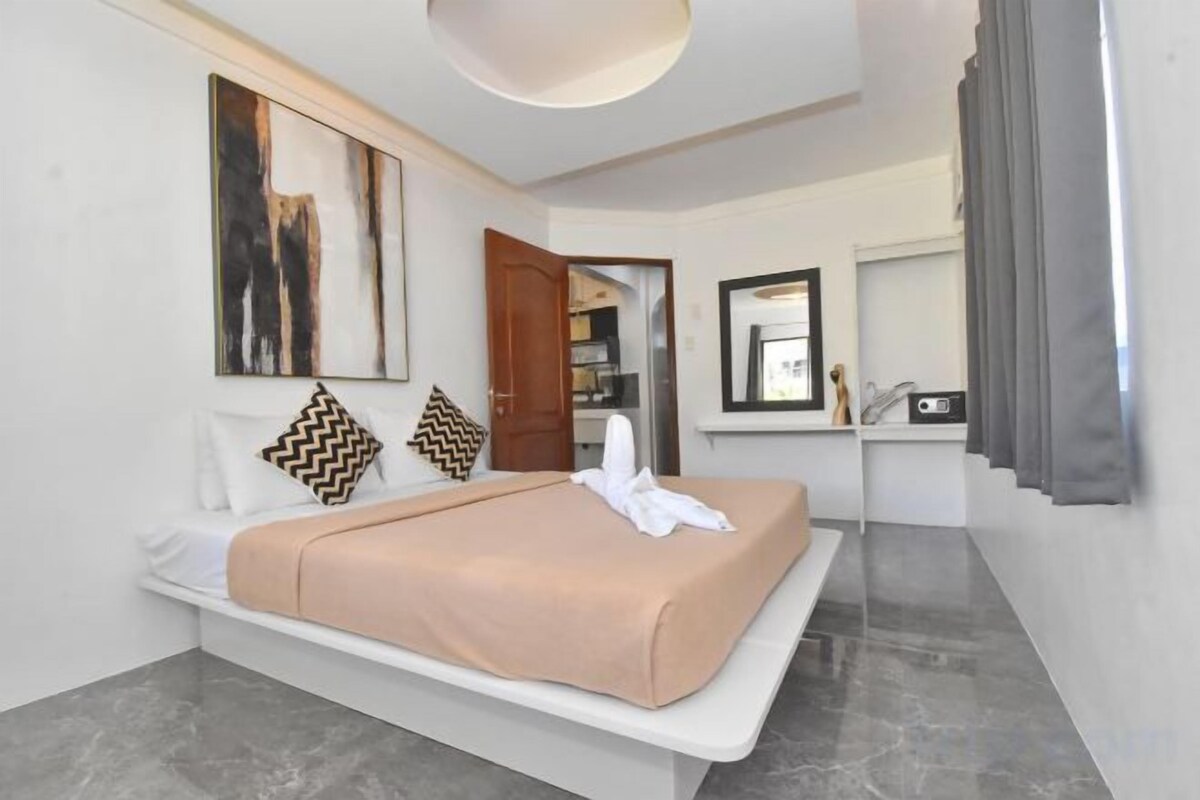 Quarto moderno com cama, espelho e porta que dá para um banheiro.