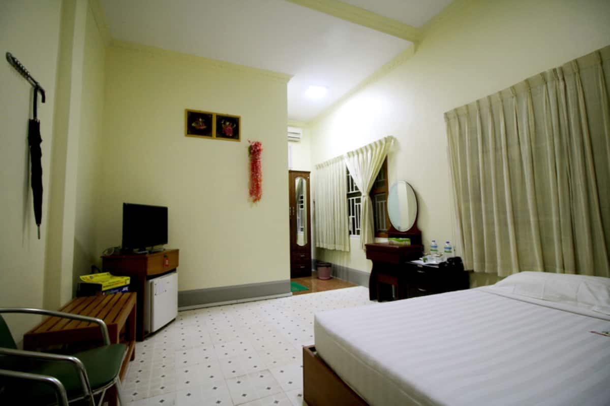 Quarto de hotel com cama, escrivaninha com computador, cadeira, televisão e espelho.