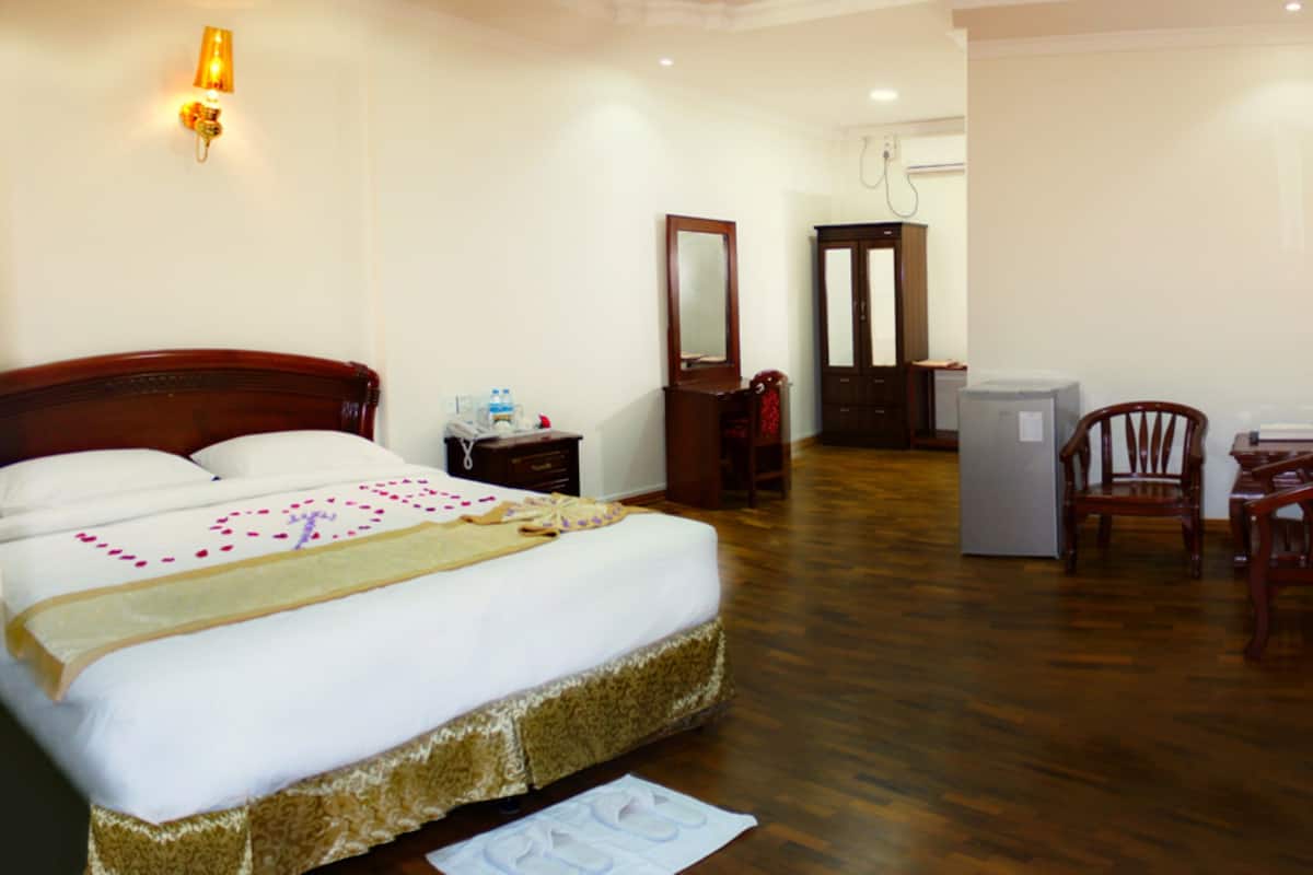 Quarto de hotel com cama, escrivaninha, cadeira, espelho, frigorífico e uma lâmpada fixada na parede.