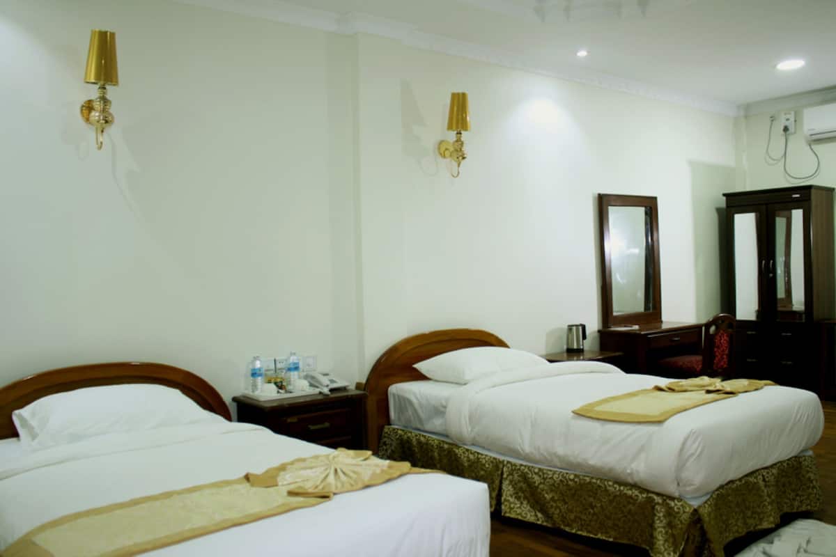 Quarto de hotel com duas camas, uma cômoda de madeira, um espelho e uma mesa de cabeceira com abajur.