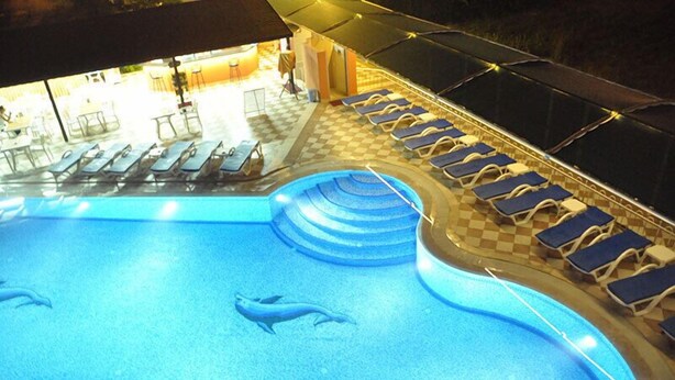 Piscina com esculturas de golfinhos, espreguiçadeiras e piso xadrez.