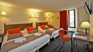 Quarto de hotel com duas camas, uma escrivaninha, uma cadeira e uma televisão na parede.