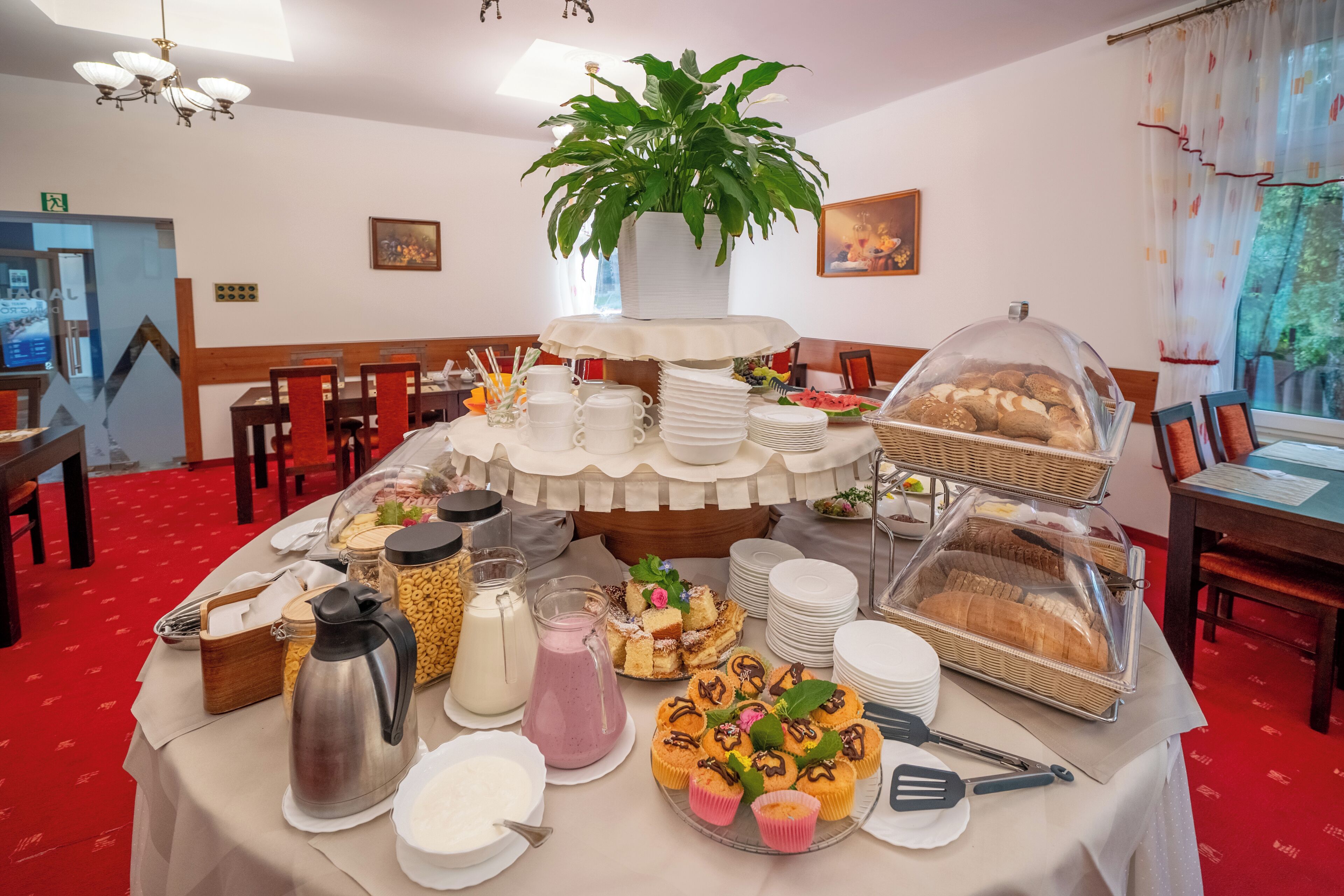 Uma mesa de buffet com diversos alimentos, uma cafeteira e uma planta.