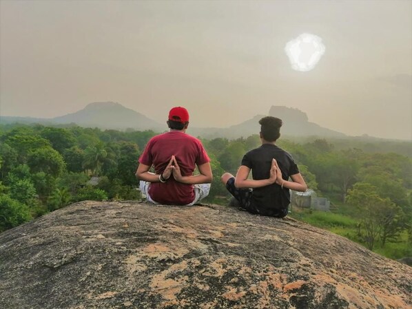 Duas pessoas sentadas em uma rocha, com uma paisagem montanhosa ao fundo.