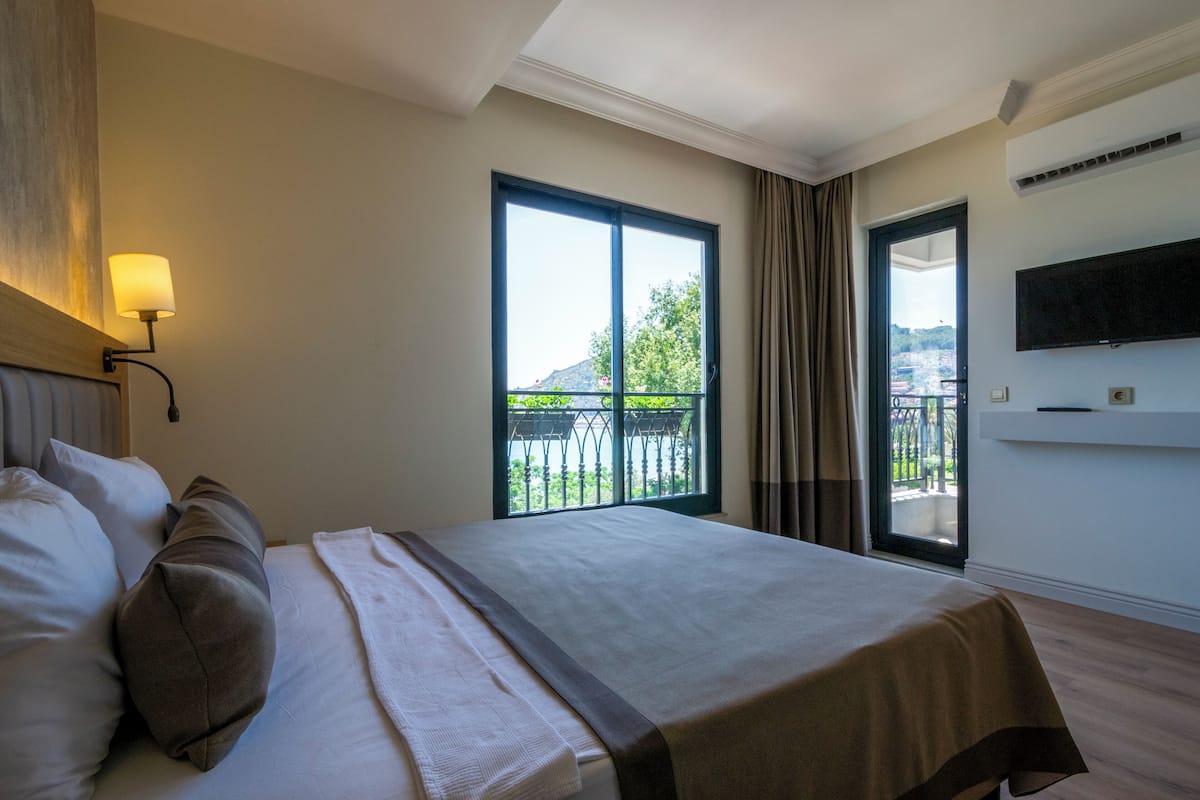 Quarto de hotel com uma cama grande, televisão na parede e varanda com vista.