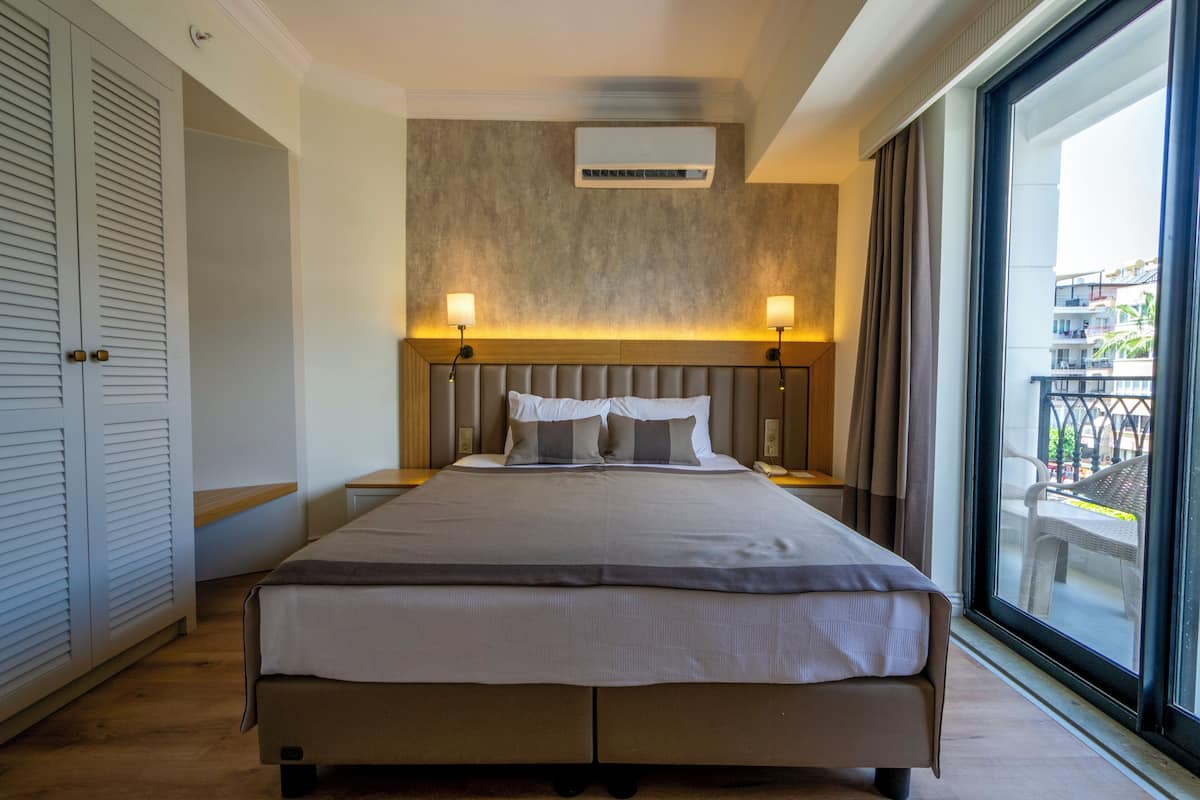 Quarto de hotel com uma cama grande, duas mesas de cabeceira, um ar condicionado e uma varanda com vista.