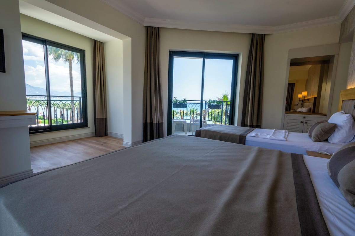 Quarto de hotel com duas camas, varanda e vista para o mar, além de uma janela grande.