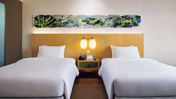 Quarto de hotel com duas camas, cabeceira de madeira, mesa de cabeceira com abajur e uma pintura abstrata moderna acima da cabeceira.