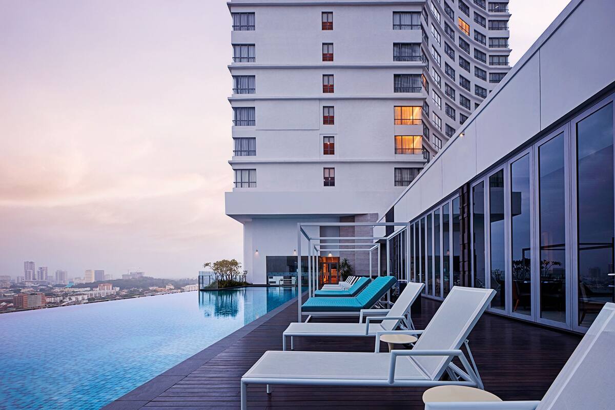 Um hotel moderno com piscina infinita no terraço, espreguiçadeiras e vista para a cidade.