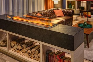 Uma sala de estar moderna com lareira de vidro, sofá de couro e estante de madeira.