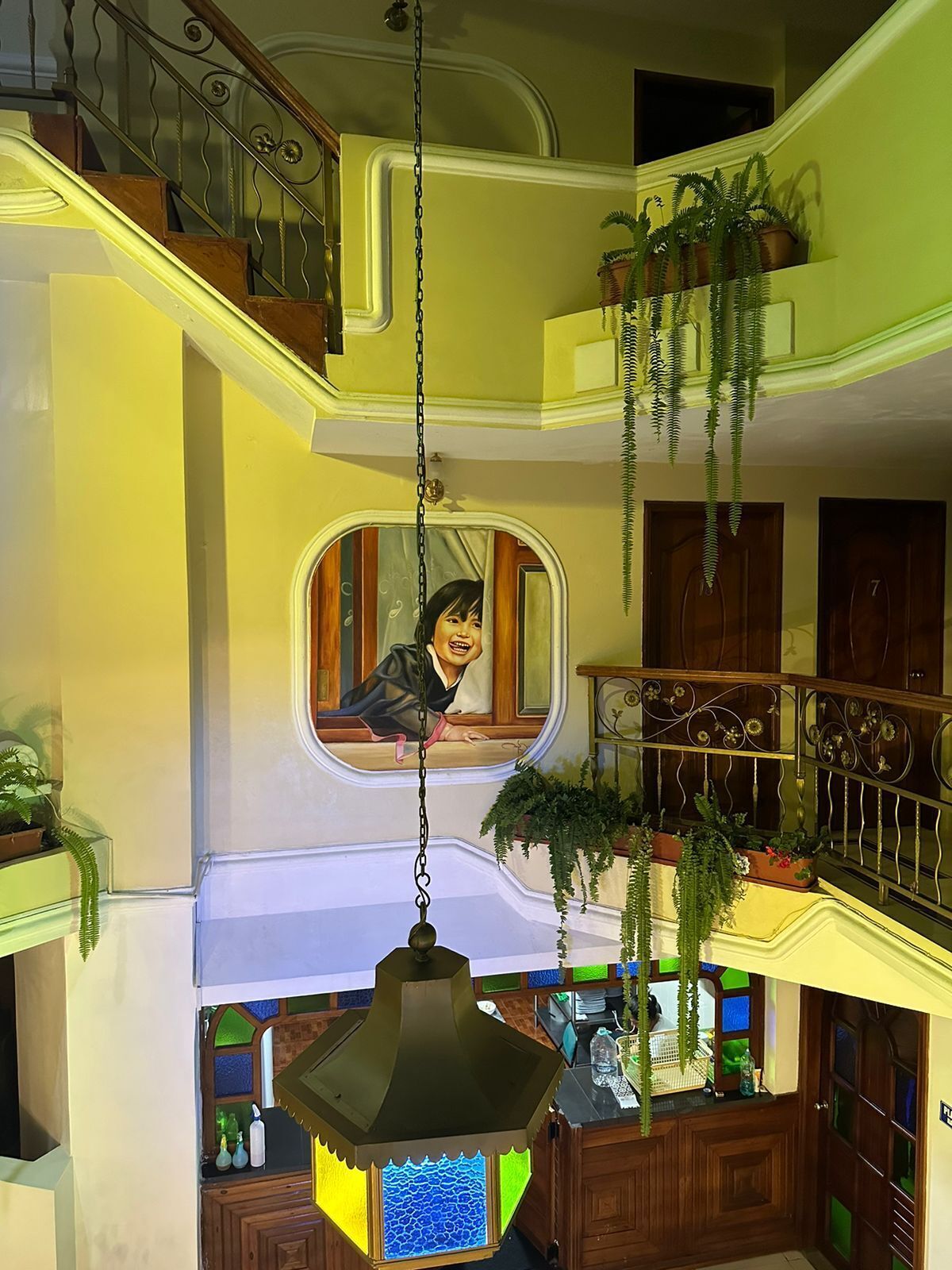 Um interior com vários níveis, uma escadaria central, um candeeiro pendente e plantas em vasos.