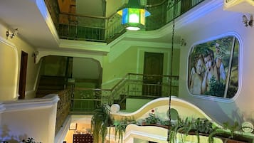 Um interior com vários níveis, com grades ornamentadas, plantas penduradas e um mural.