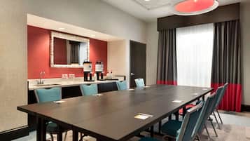 Uma sala de conferências com uma mesa comprida, cadeiras, um canto para café e uma janela grande com cortinas.