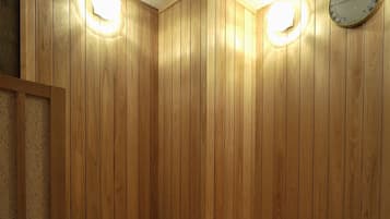 Uma sauna com paredes e bancos de madeira, duas luzes fixadas na parede e um relógio.