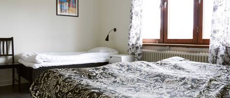Quarto com cama, cadeira, escrivaninha, radiador e janela com cortinas.