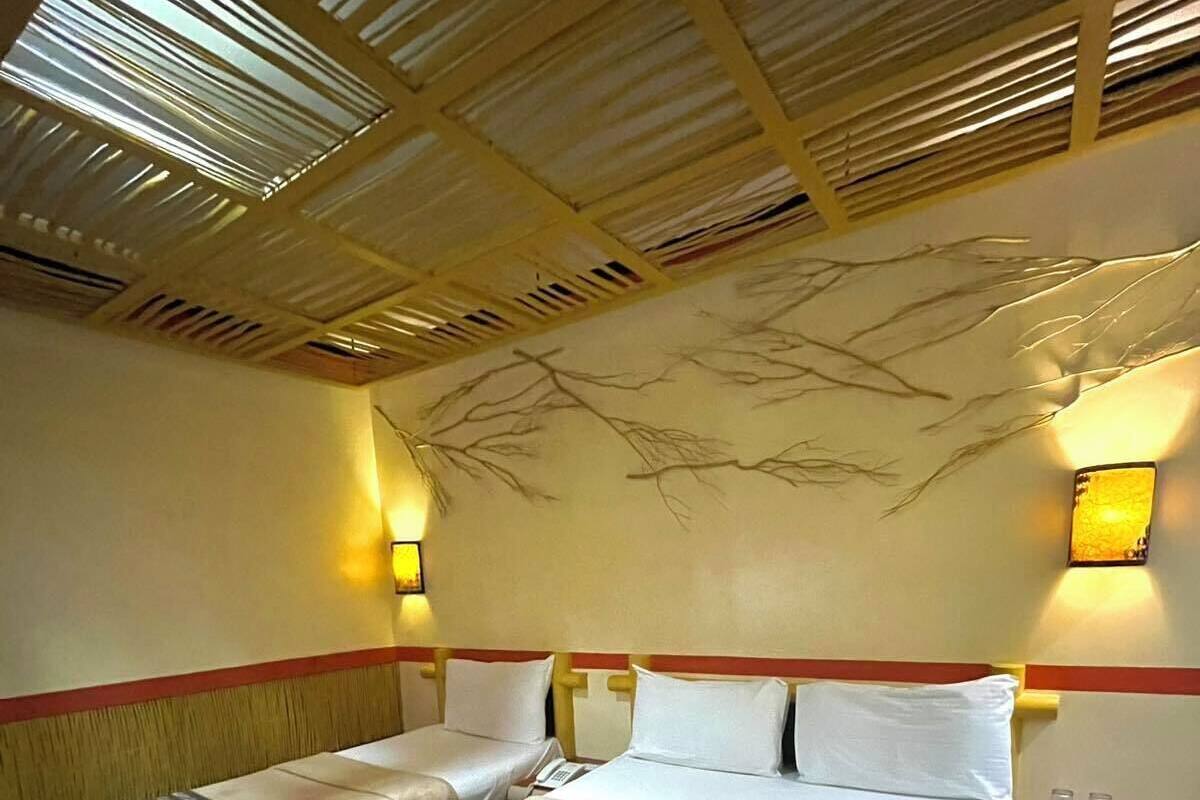 Quarto de hotel com uma cama grande, duas mesas de cabeceira e uma luminária fixada na parede.