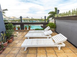 Terraço no telhado com duas poltronas brancas, uma piscina e plantas em vasos.