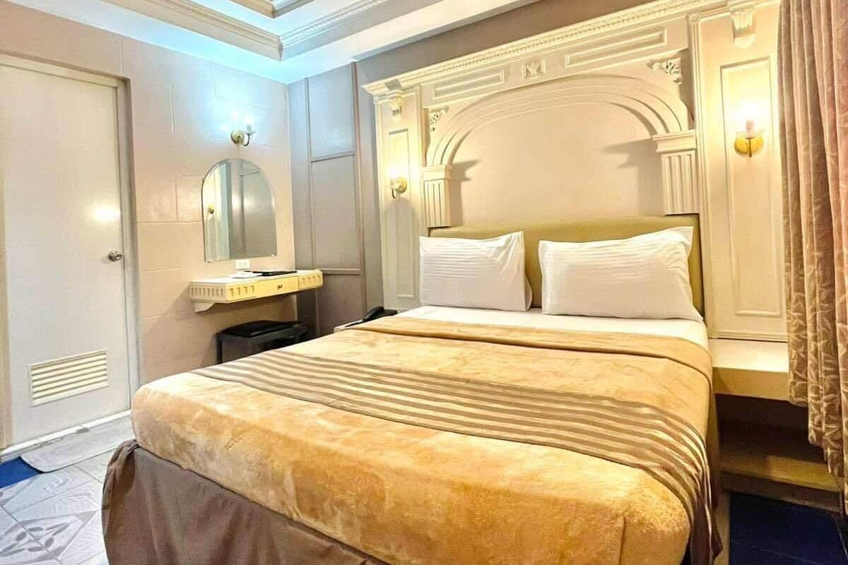 Quarto de hotel com uma cama grande, mesa de cabeceira, espelho e luminária na parede.