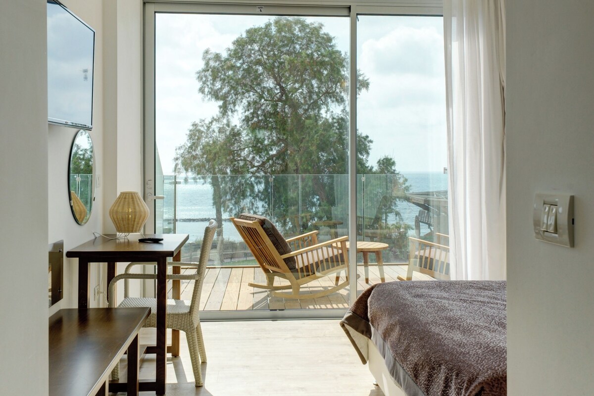 Quarto com uma grande porta de correr de vidro que dá para uma varanda com vista para o mar e para árvores.