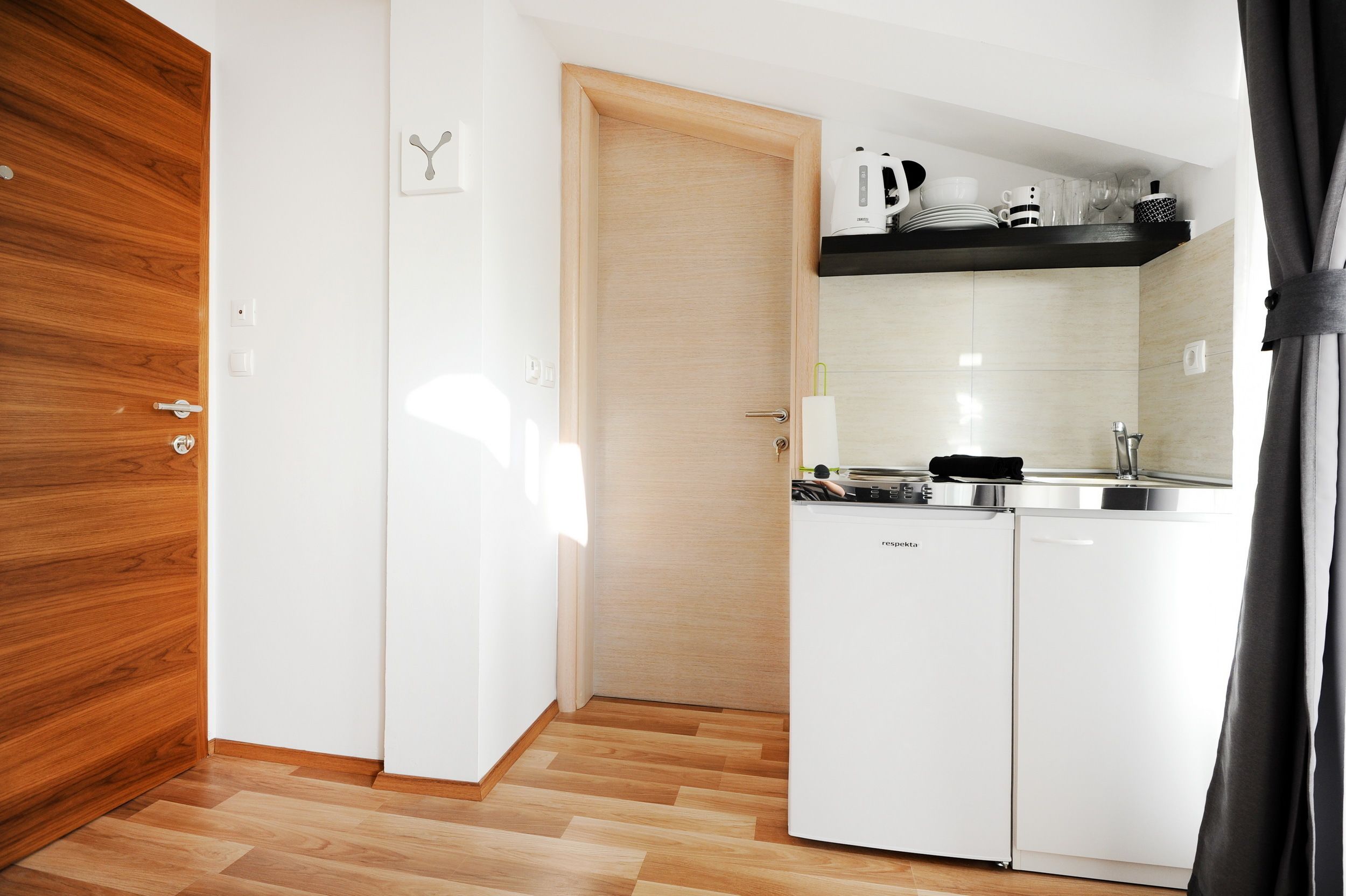 Cozinha compacta com geladeira branca, pia e porta de madeira.
