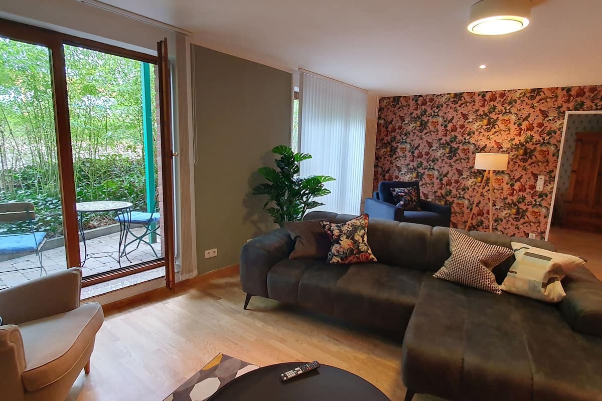 Uma sala de estar com sofá, poltrona e um espaço de jantar com mesa e cadeiras.