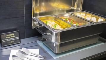 Disposição de buffet com recipientes etiquetados para diferentes refeições quentes, incluindo um aviso que indica os tipos de comida disponíveis.