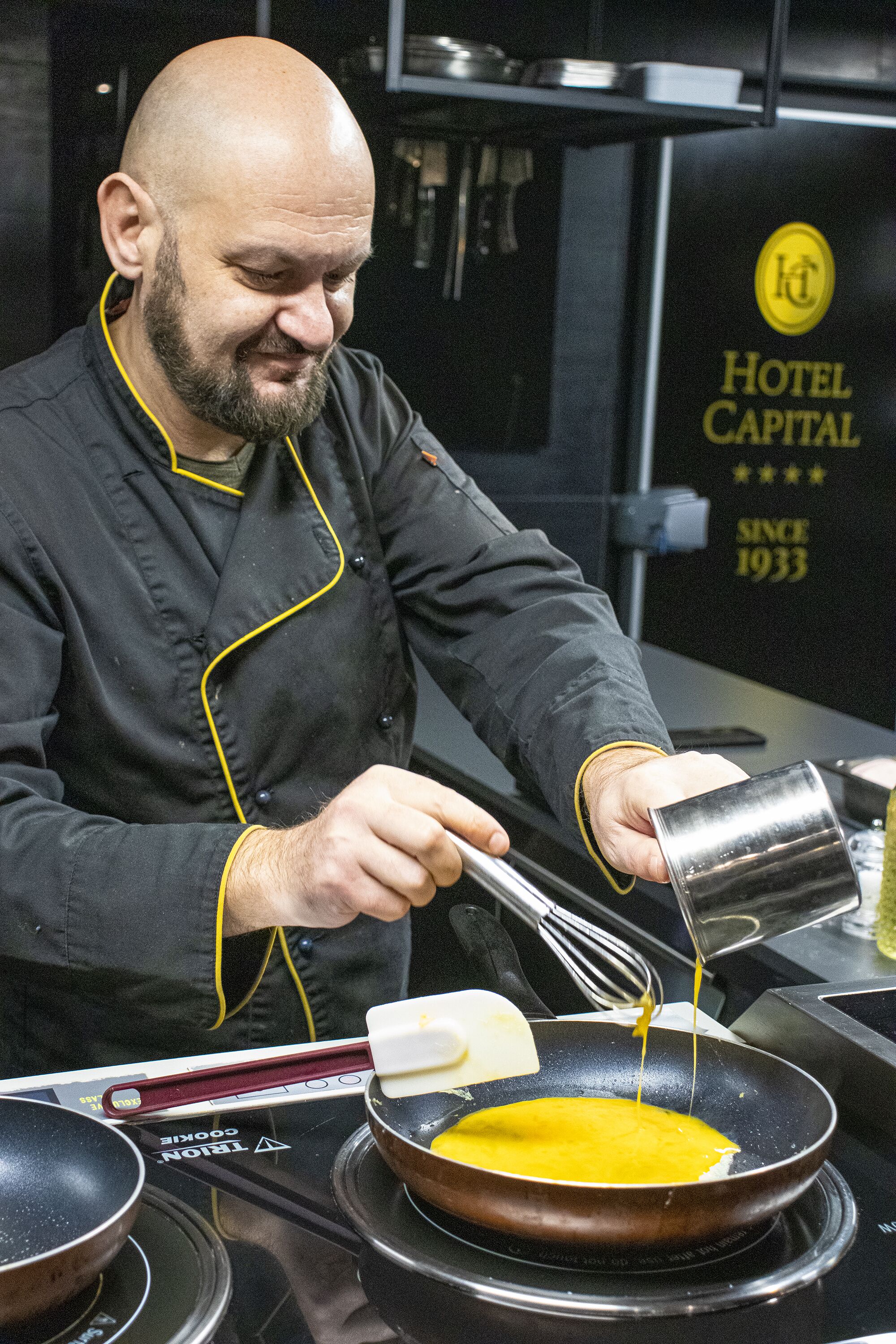 Um cozinheiro prepara comida em uma cozinha, com uma placa que indica que o estabelecimento está em funcionamento desde 1933.