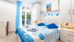Quarto com cama, escrivaninha, cadeira, janela com cortinas e vista para o exterior.